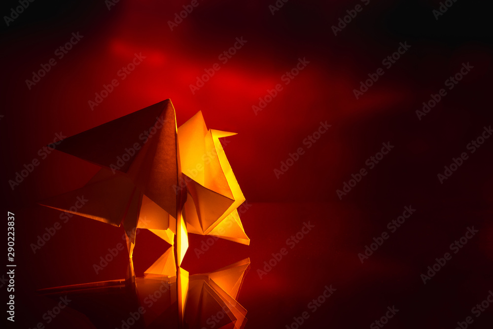 Origami. Paper dragon on red background. The light falls on the figure ...