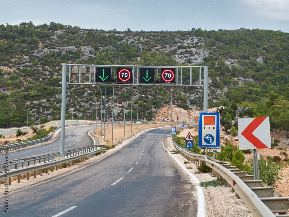 Asphalt road with many road signs and metal arch with direction arrows ...