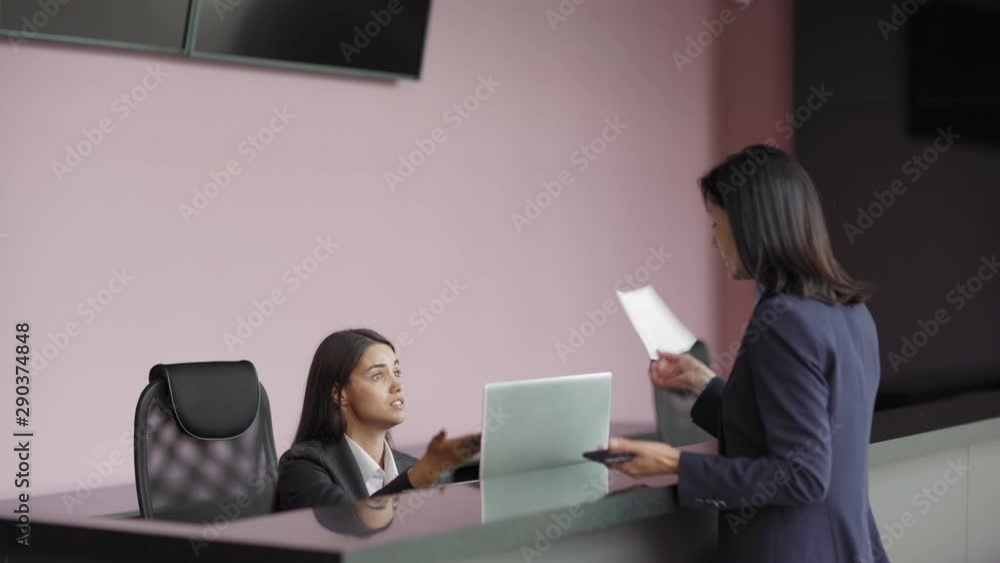Middle aged businesswoman arguing with young receptionist at counter in ...