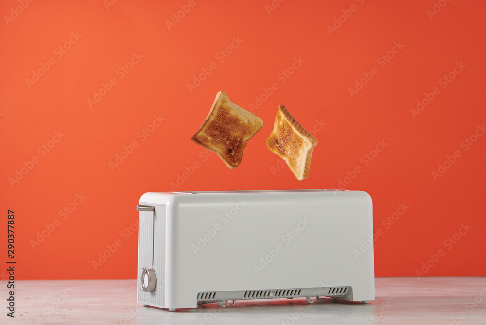 Roasted toast bread popping up of toaster with red wall, front view ...
