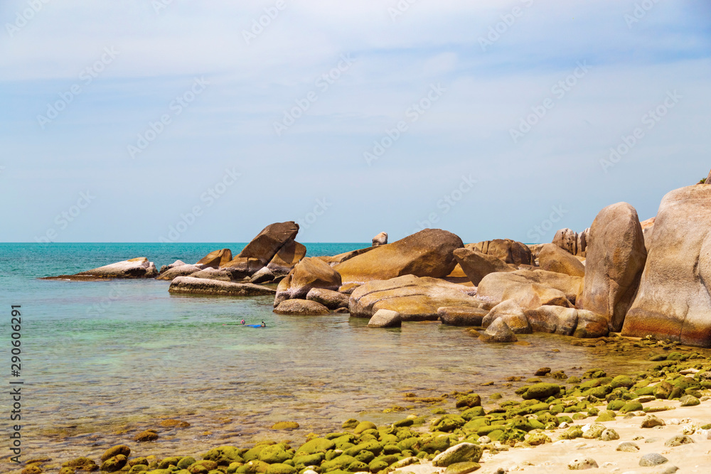 Big yellow rocks in the sea against the blue sky. Floating man in mask ...