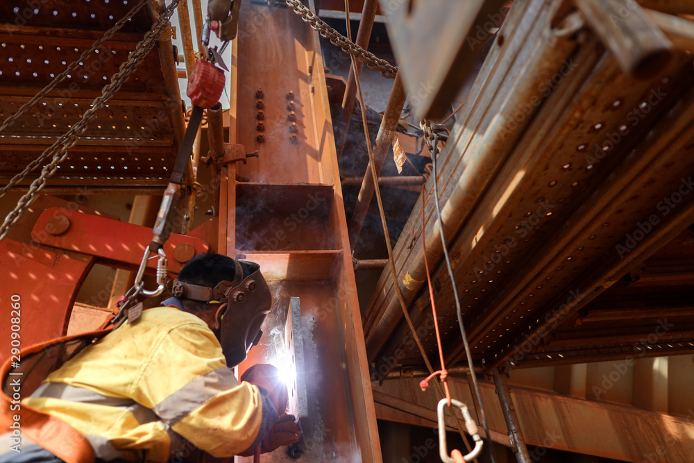 Construction worker welder wearing safety helmet, fall arrest harness ...