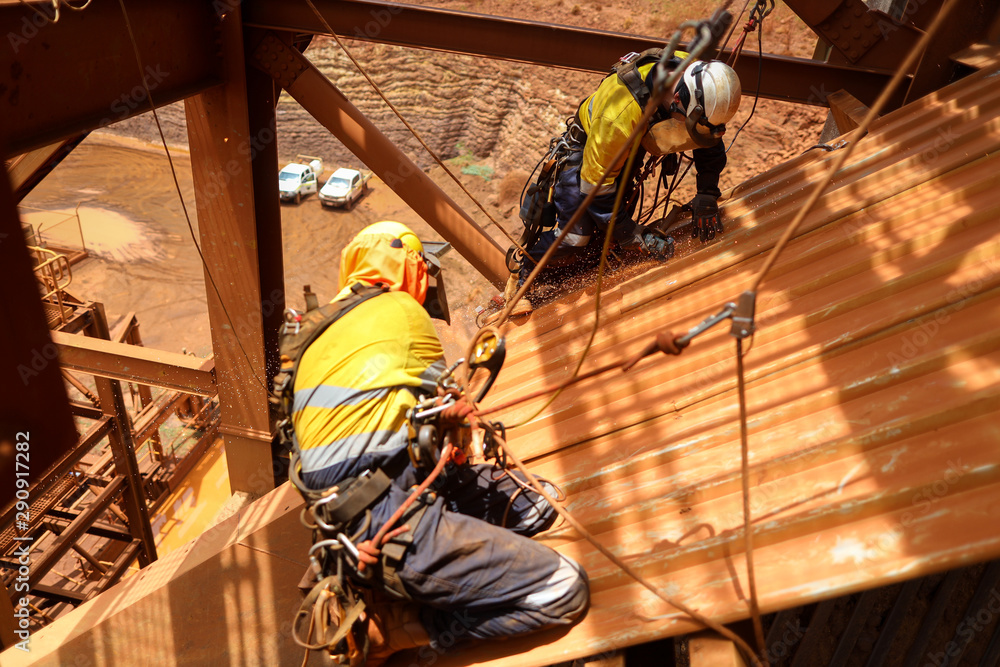 Two rope access maintenance abseiler wearing safety harness, helmet ...