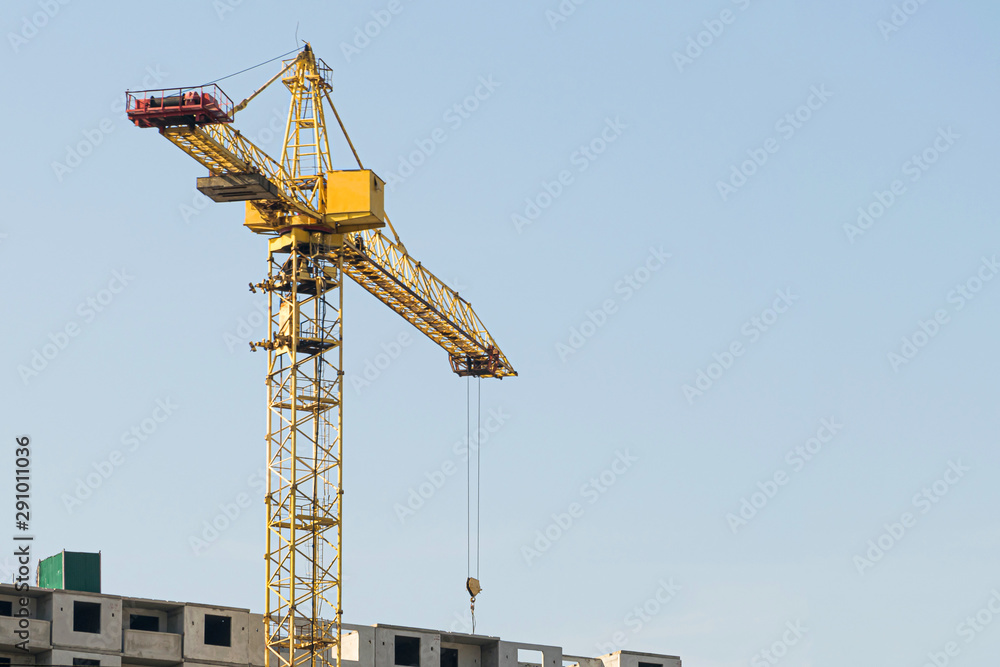 A yellow high-rise building crane against a blue sky builds multi ...