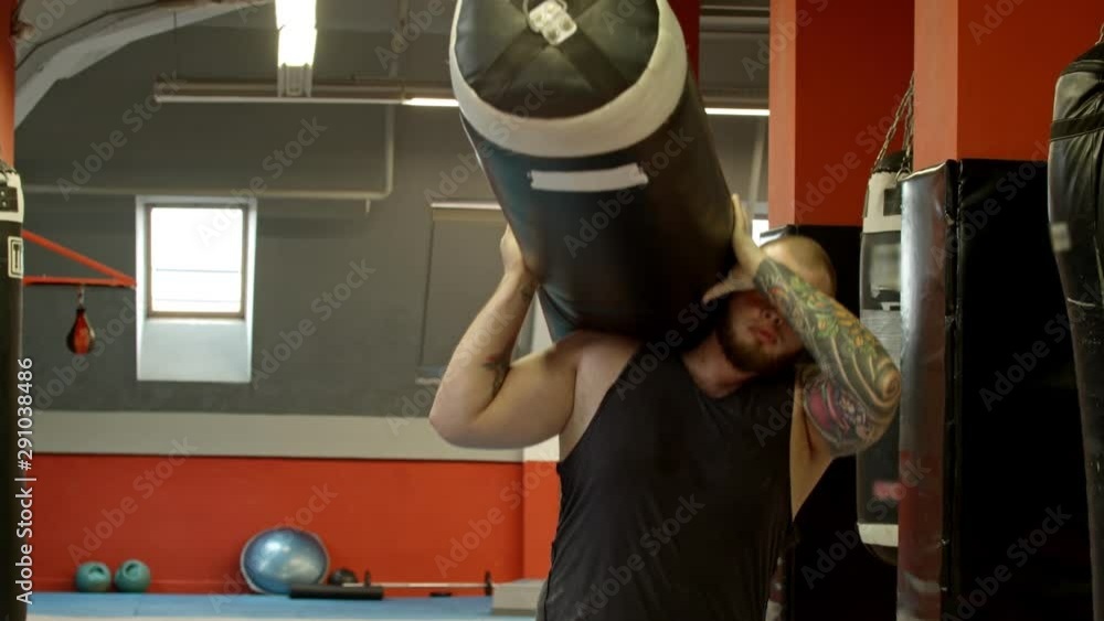 A man bodybuilder carrying the punching bag on the shoulder and puts it ...