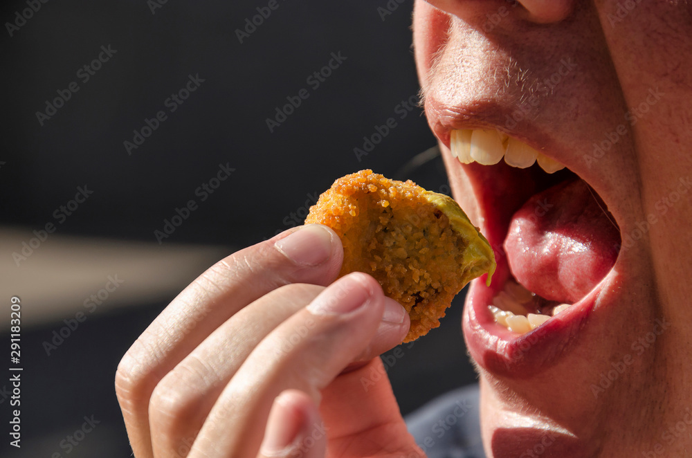 Human hand bringing a traditional Dutch bitterbal (meatball) dipped in ...