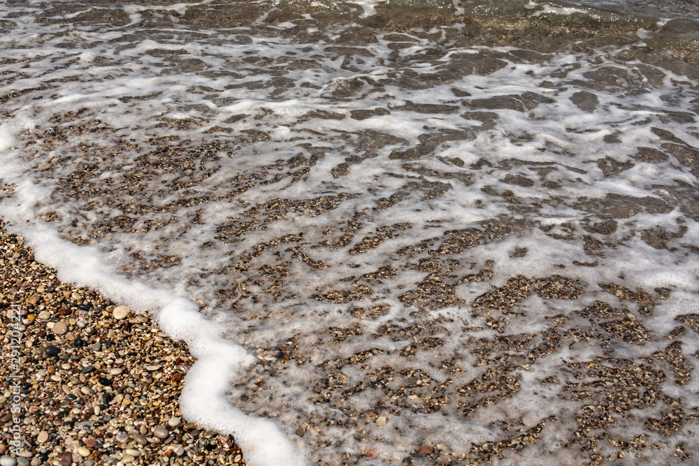 Sea water runs to the rocky shore and rolls, leaving a foamy trail. The ...