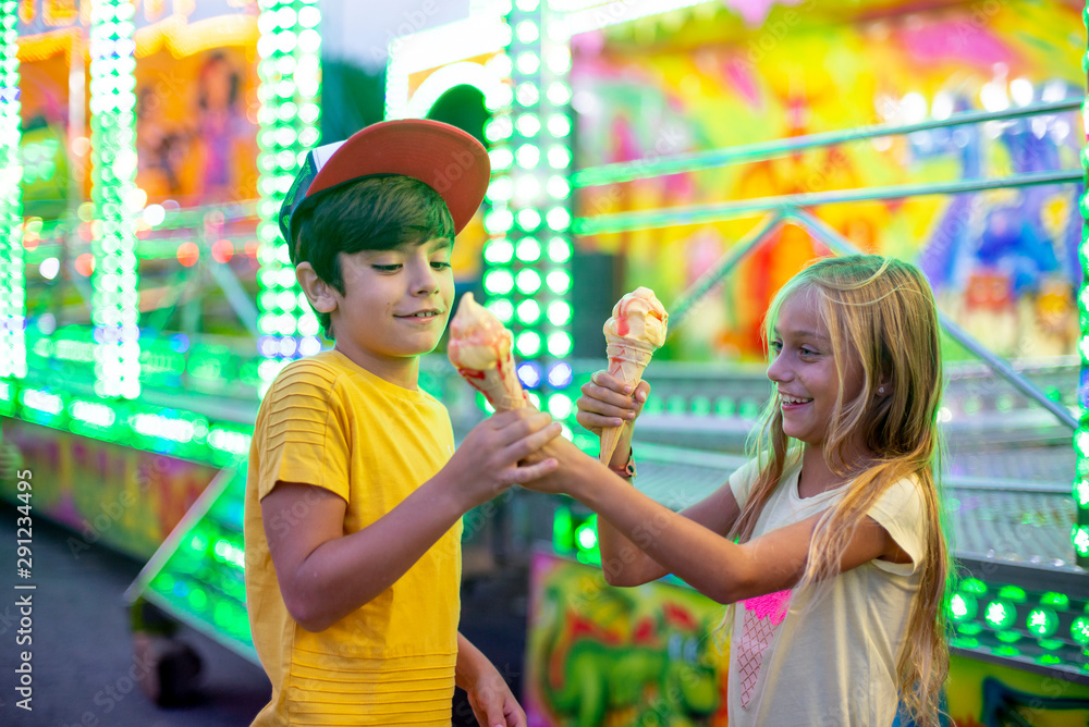 Smiling girl and boy eating ice cream in Funfair Park lights carnival ...