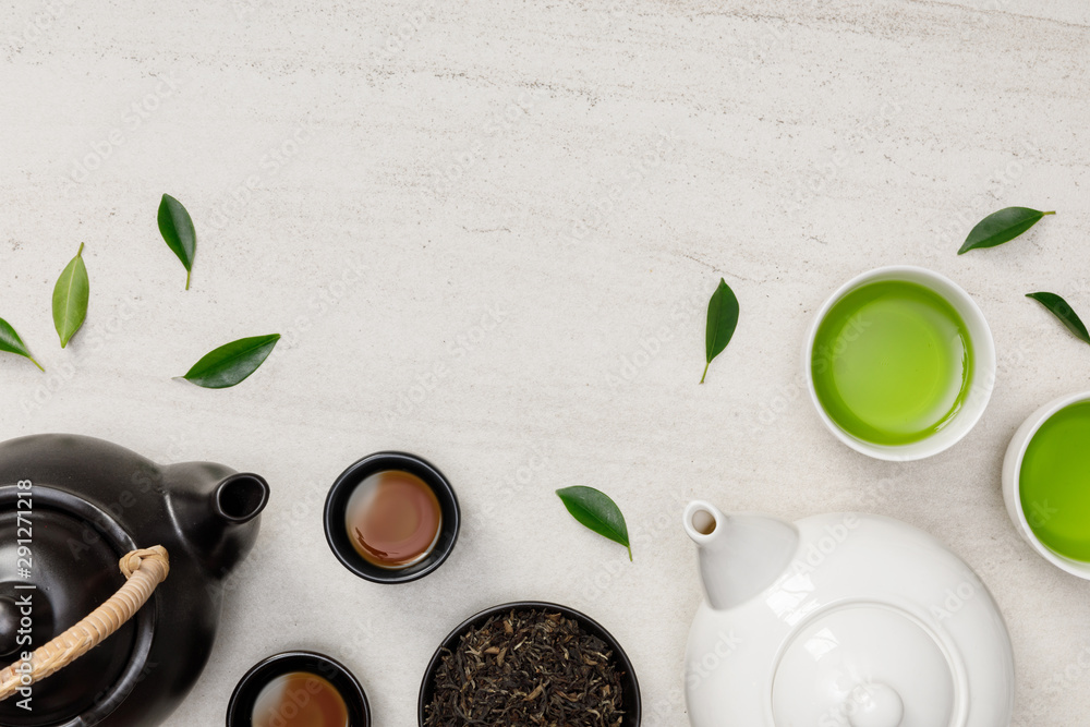 Cup of hot tea with teapot, green tea leaves and dried herbs top view ...