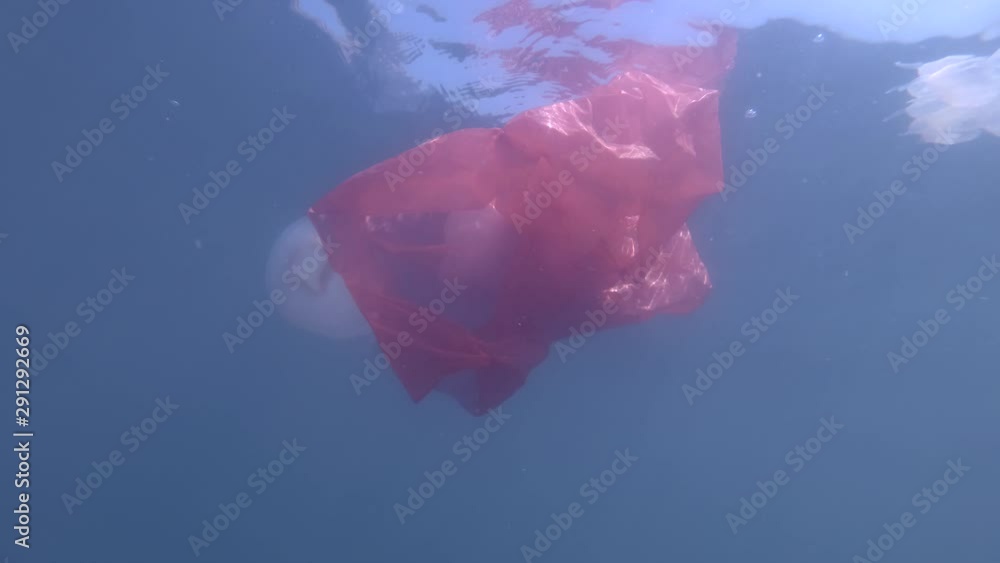 Plastic pollution, a discarded red plastic bag slowly drifting with ...