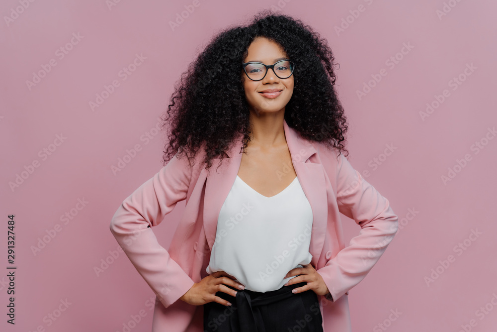 Waist up shot of satisfied dark skinned female office worker keeps ...