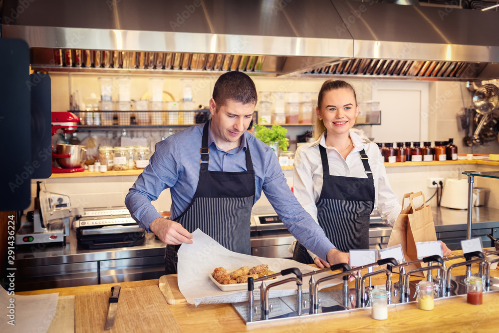 Cheerful waiters wearing apron serving takeaway food at counter in fast ...