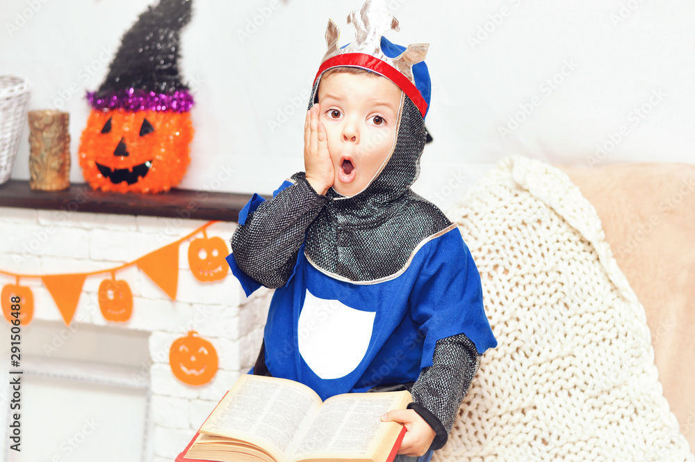 Little surprised boy in a knight costume with a crown on his head sits ...