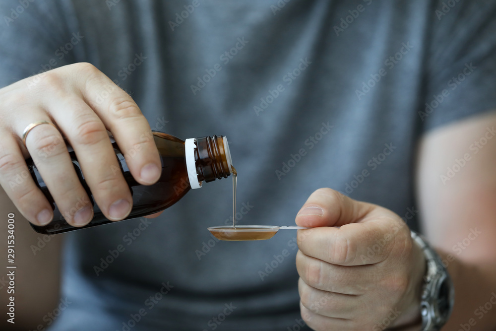 Fotka „Focus on male hands holding bottle of cough syrup and measuring ...