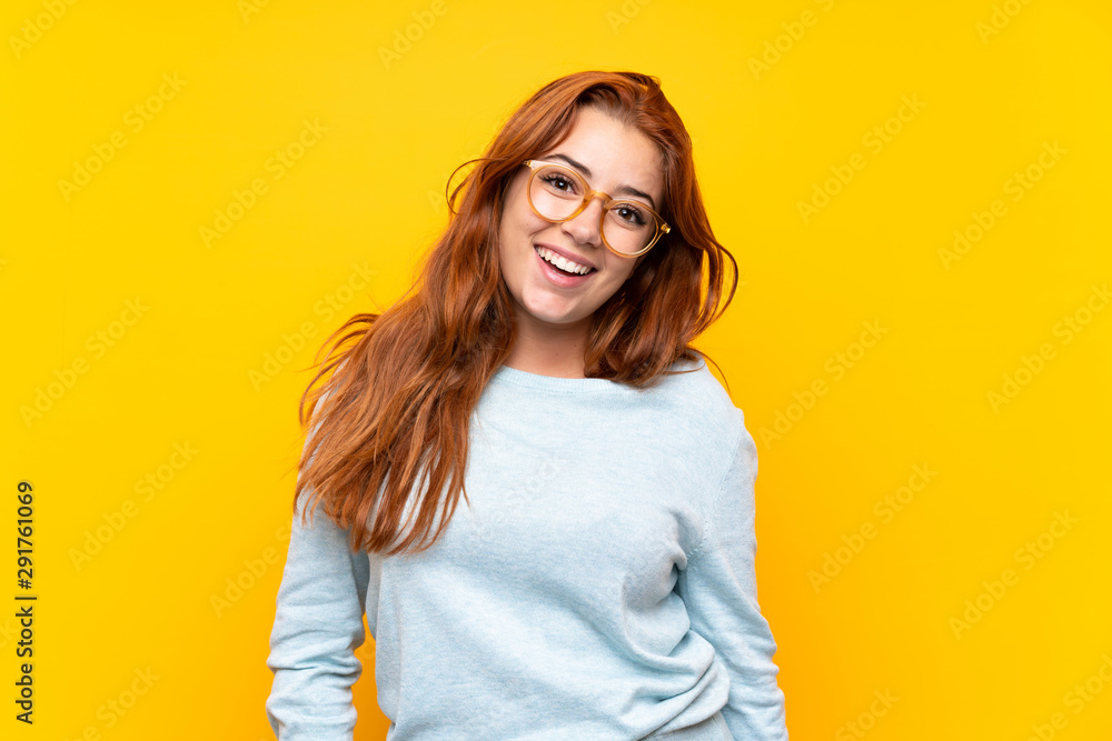 Teenager redhead girl over isolated yellow background with glasses and ...