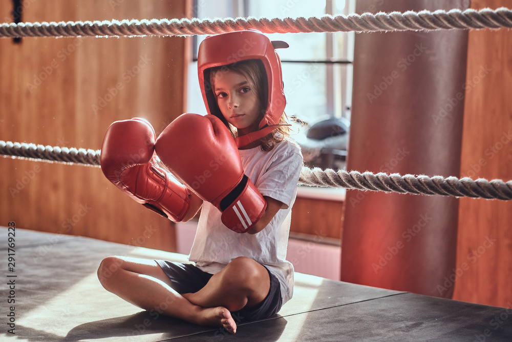 Beautiful kid girl is sitting on boxing ring wearing boxer uniform ...