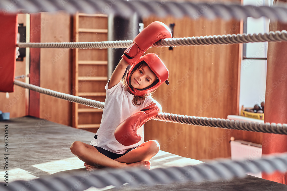 Beautiful kid girl is sitting on boxing ring wearing boxer uniform ...