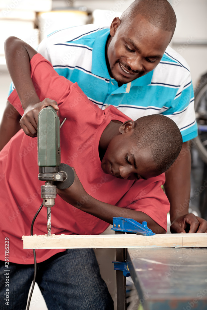 African Father and son using a drill in a workshop Stock Photo | Adobe ...