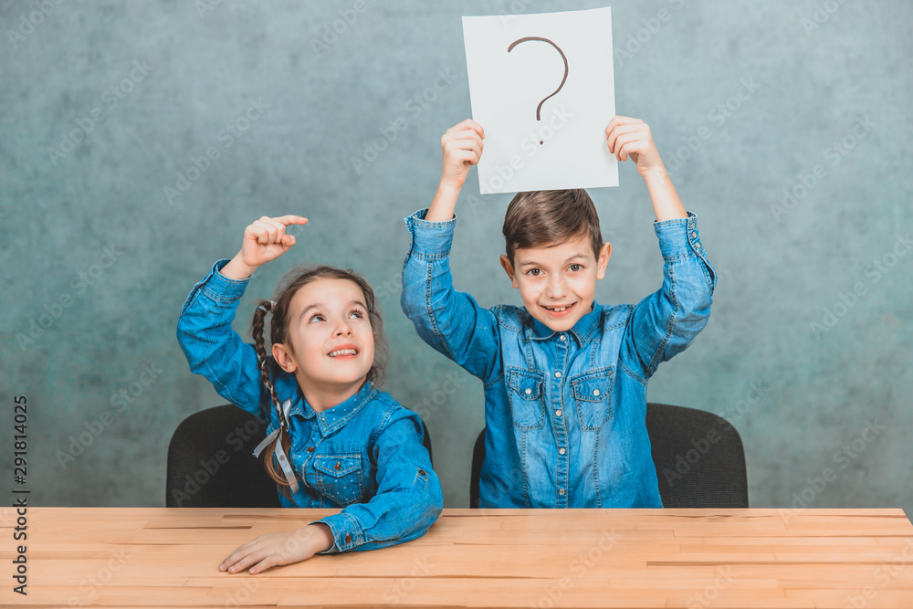 Schoolchildren sitting at the desk. Boy is raising up the sheet of ...