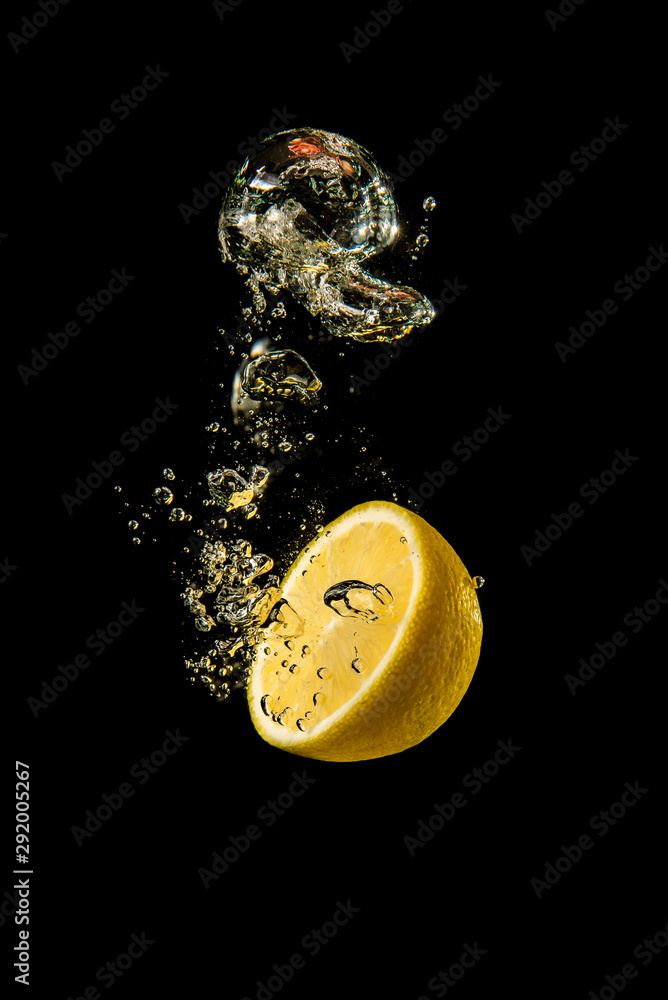Fresh yellow lemon half in water splash on black background with lots ...