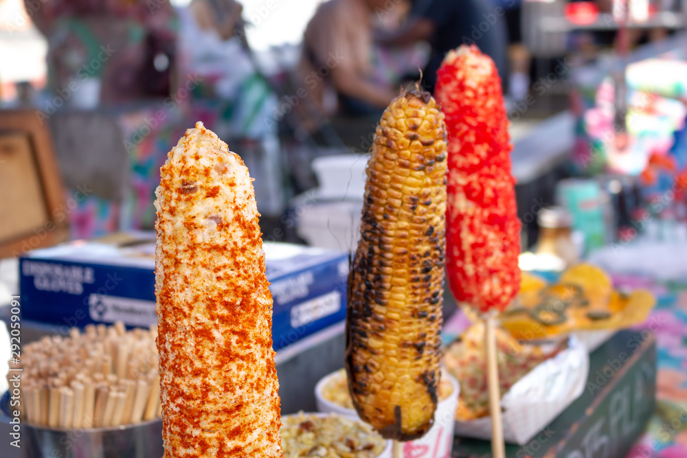 Several varieties of Mexican elote snacks on display at a food stand ...