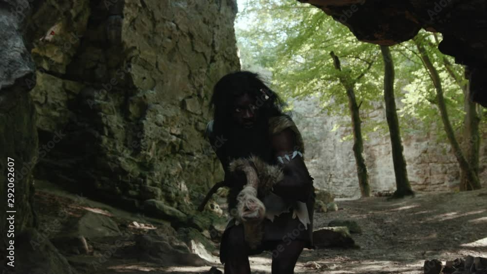 Primitive black neanderthal wildman walking with stick in rocky ...