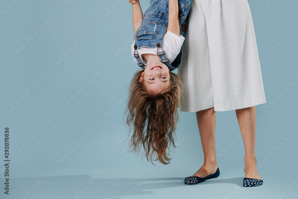 Mother is holding her laughing daughter upside down over blue ...