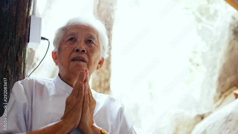 An Asian old lady, a Buddhist, has white hair, white clothes, sitting ...