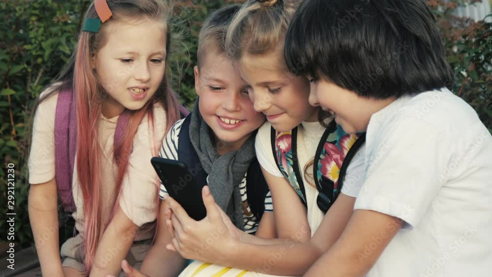 Fun with phone. Two little school girls and two boys using smart phone ...