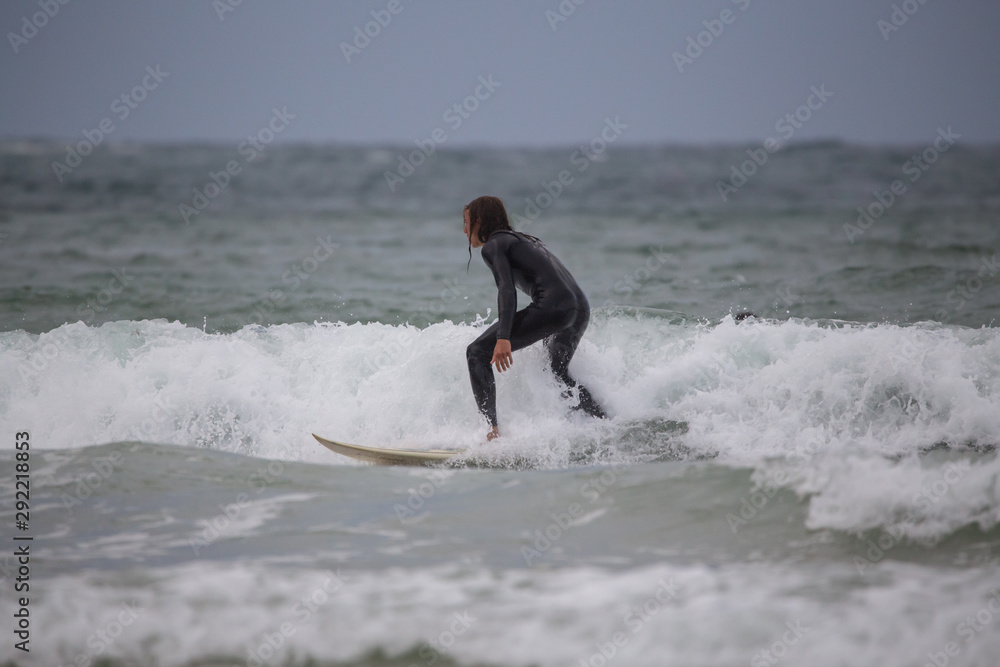 Poster Side view of sportsman in black wetsuit surfing on white board ...