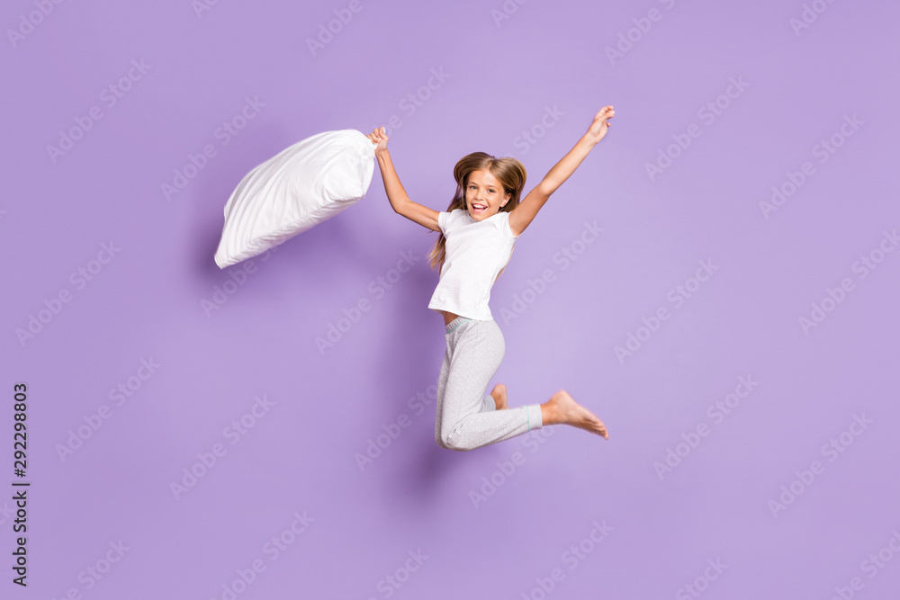 Full length photo of funky funny kid jump raise pillow have fun on ...