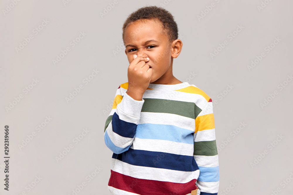 Displeased dark skinned 8 year old boy grimacing and pinching nose ...