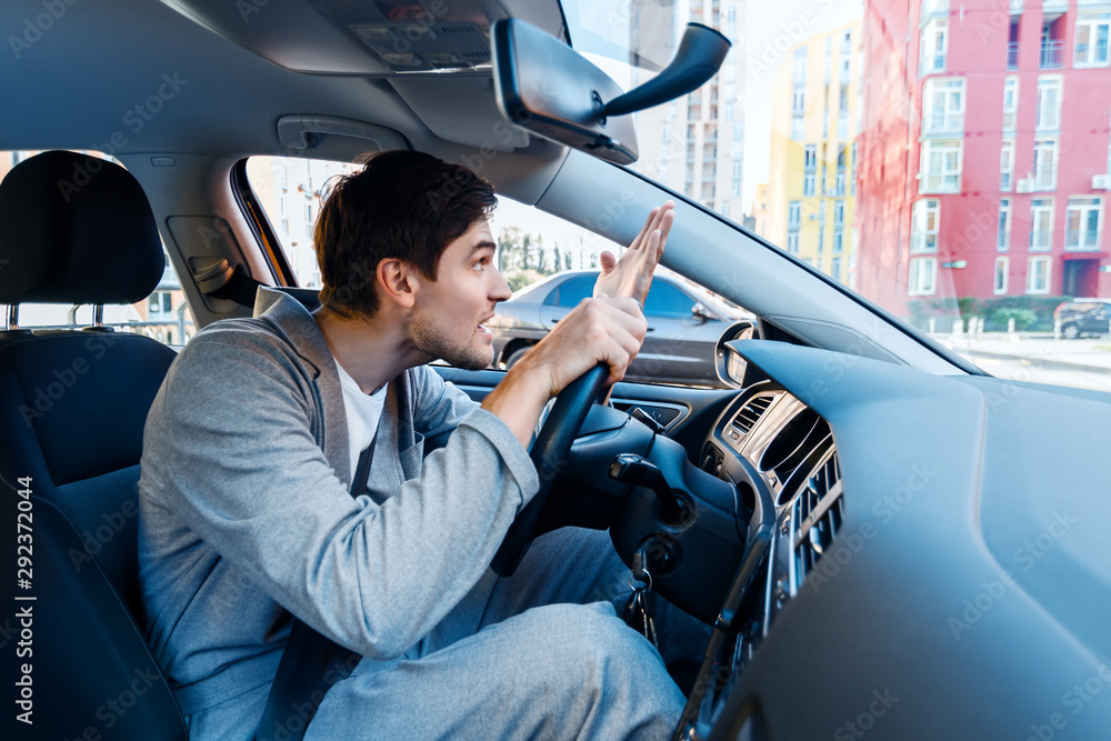 Annoyed young businessman is driving car. Man in gray suit is swearing ...