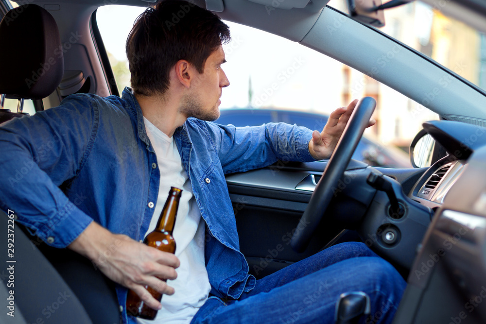 Young brunette man is drinking beer behind steering wheel of car. Drunk ...