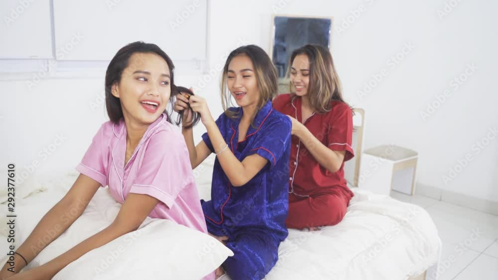 Group of beautiful teenage girls sitting on the bed while tying the ...