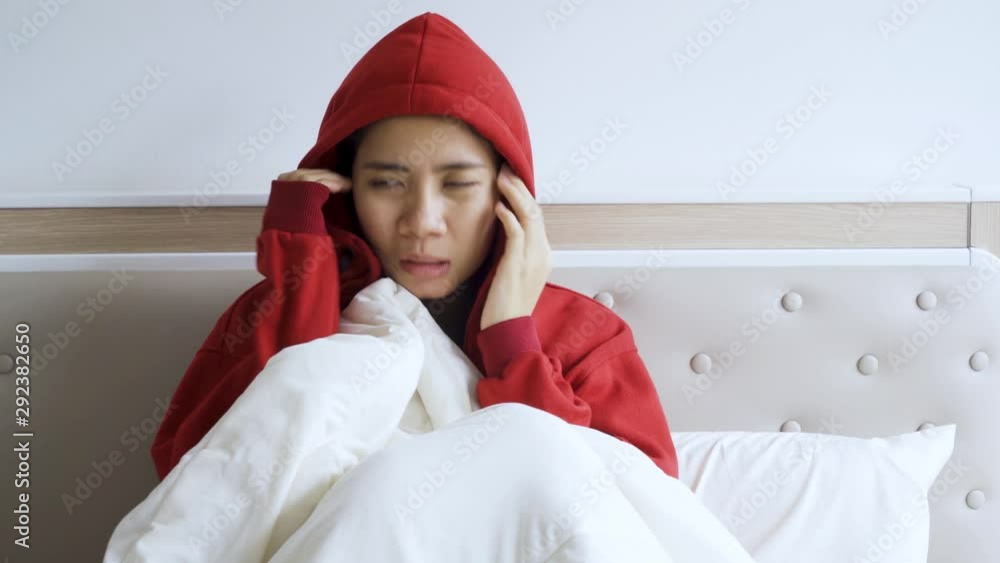 Sick woman sitting on the bed while shivering and wearing jacket in ...