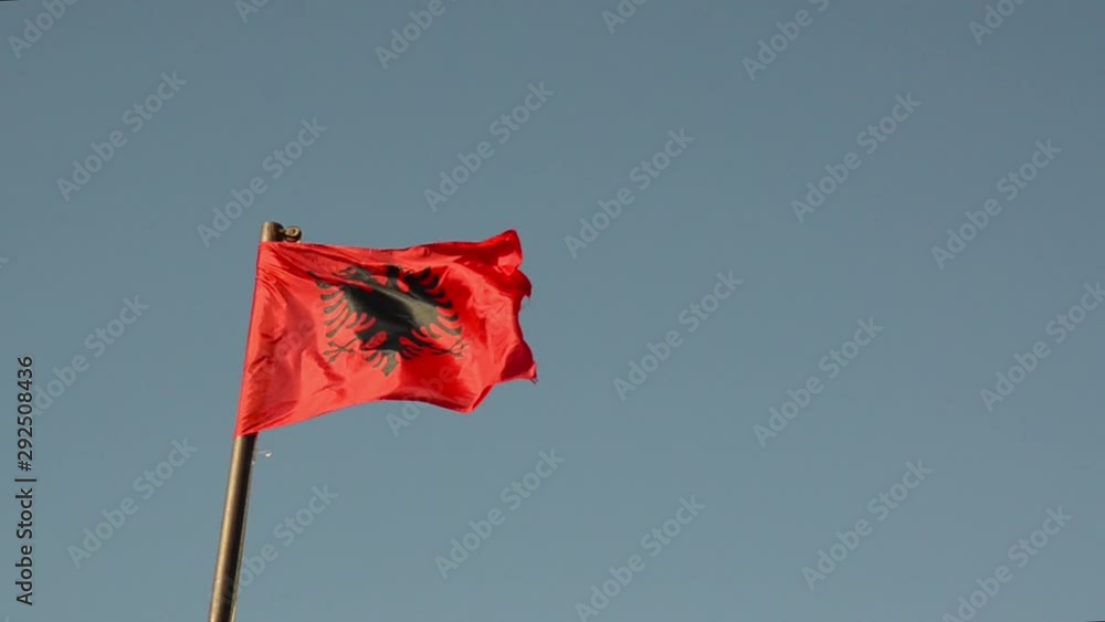 Albanian national flag flying on a flagpole against blue sky. State and ...