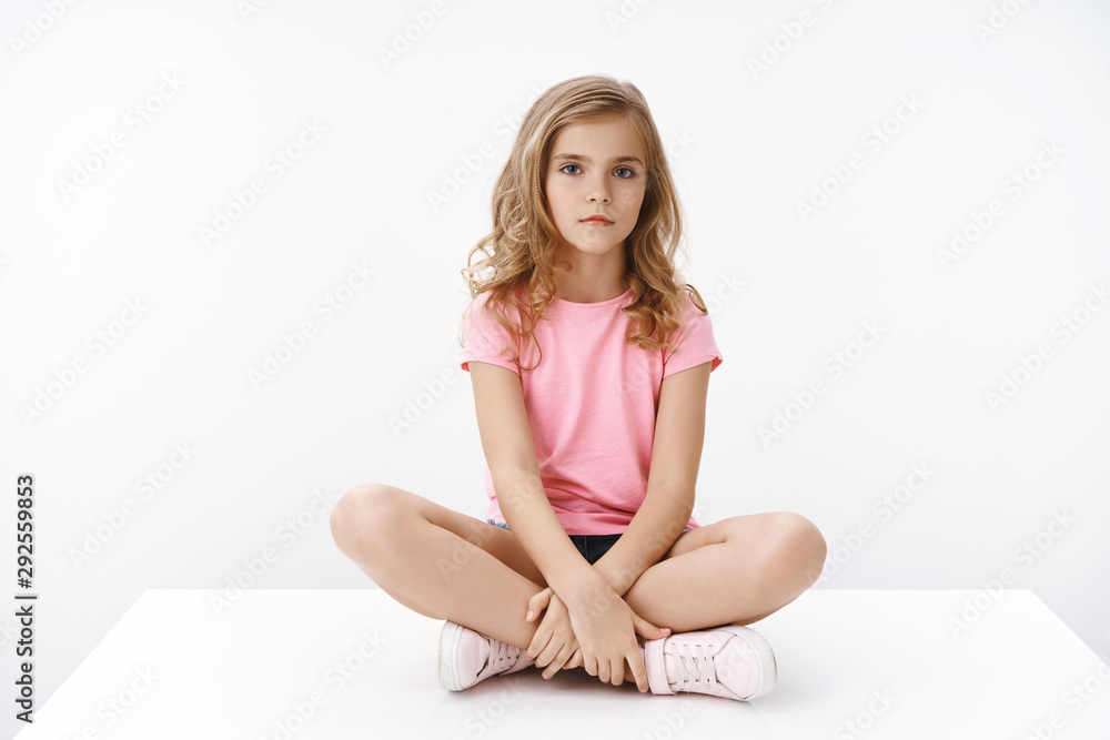 Serious indifferent cute blond little girl sitting on floor, legs ...