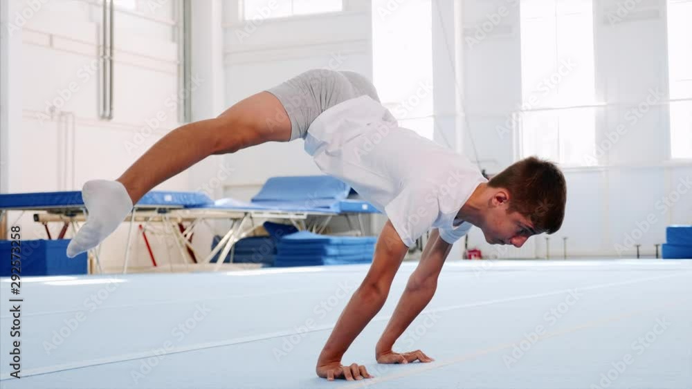 A young athlete boy is making a side split in a handstand and lands on ...