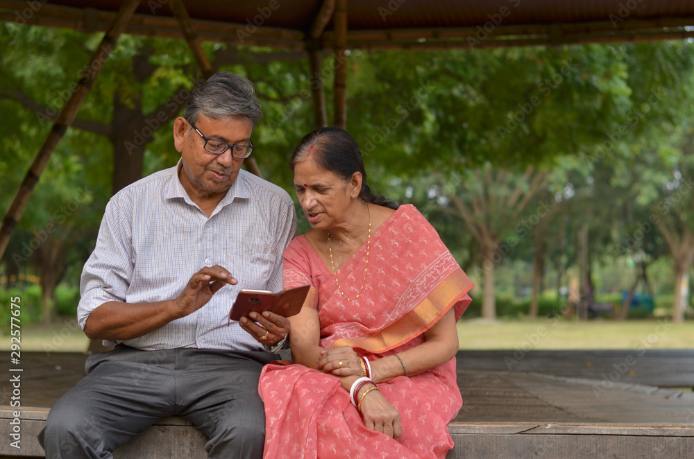 Senior citizen Indian couple reading from mobile, smiling and laughing ...