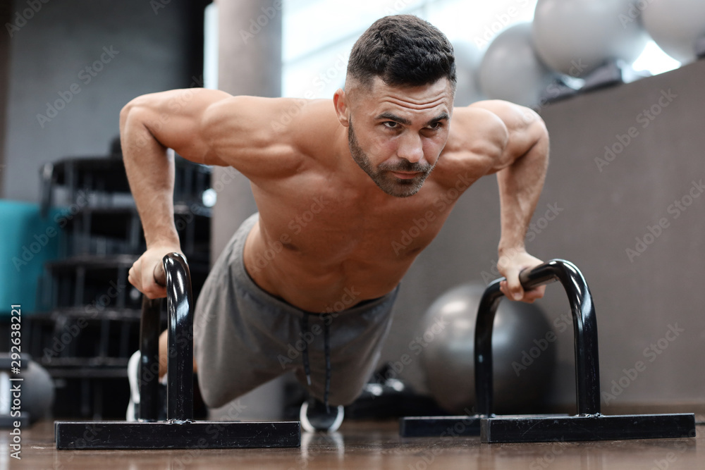 Fit and muscular man doing horizontal push-ups with bars in gym. Stock ...