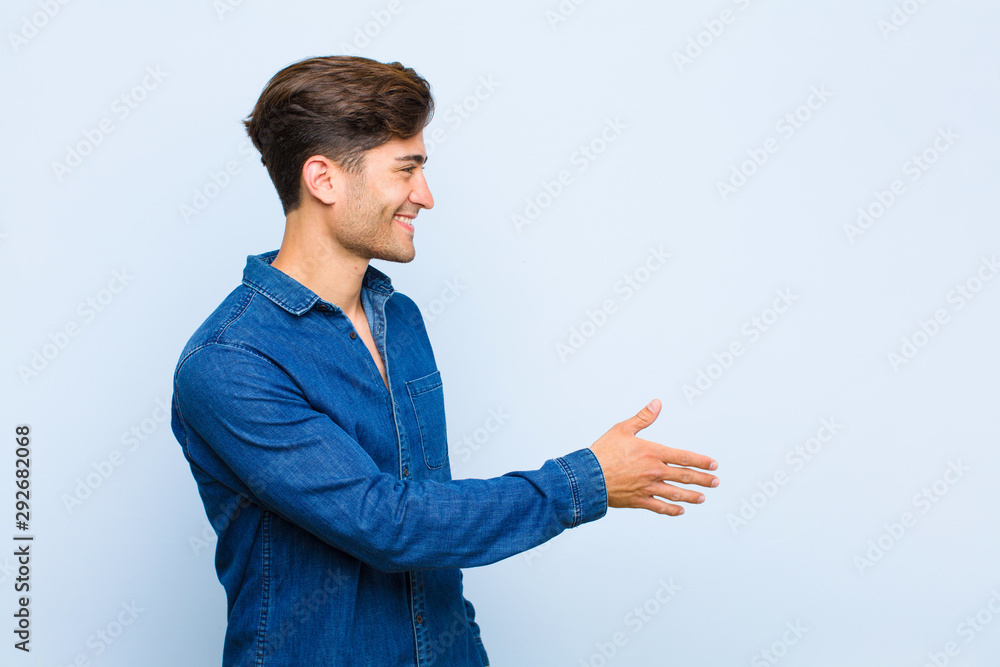 young handsome man smiling, greeting you and offering a hand shake to ...