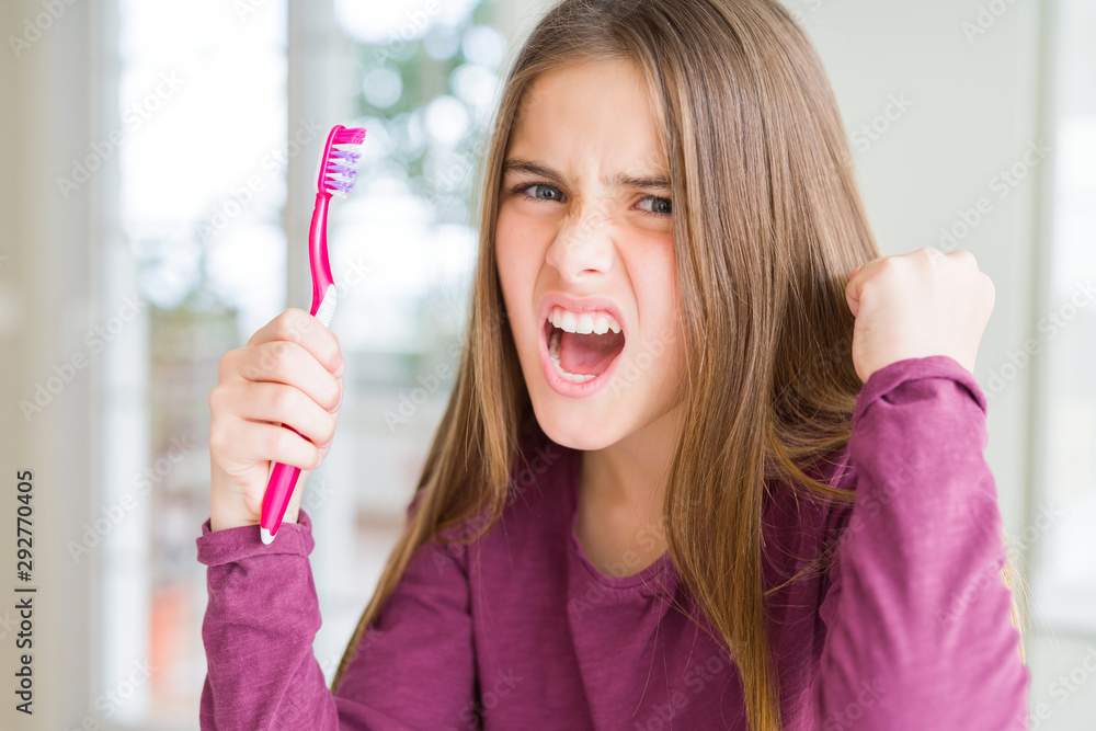 Beautiful young girl kid holding pink dental toothbrush annoyed and ...