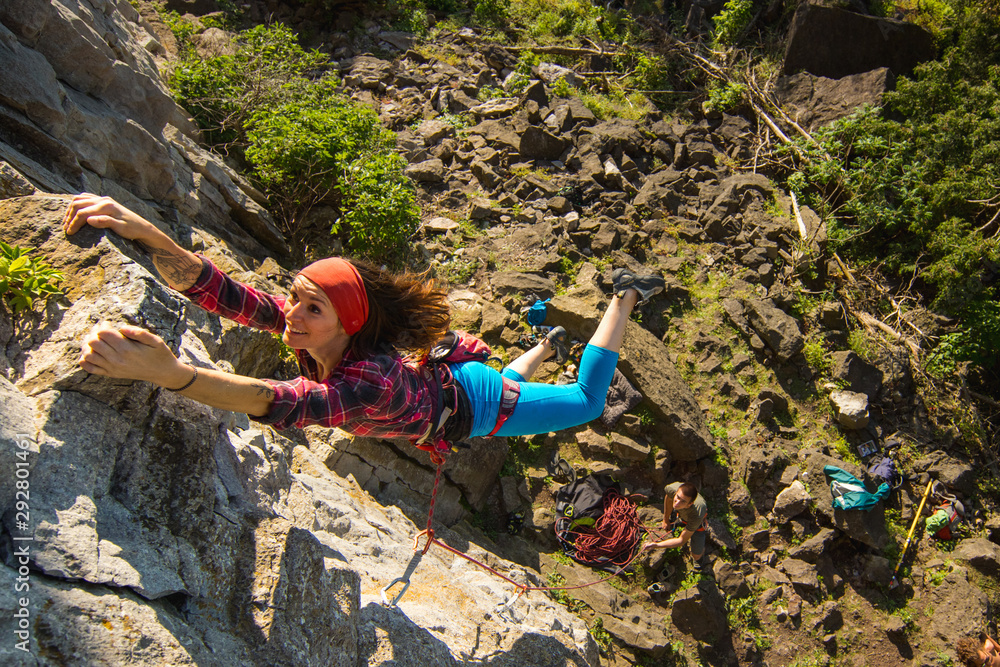 Rock climber hanging off the side of a cliff with her feet dangling ...