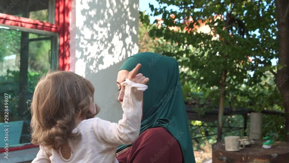 Young beautiful mother in hijab hugs and kisses his little daughter ...