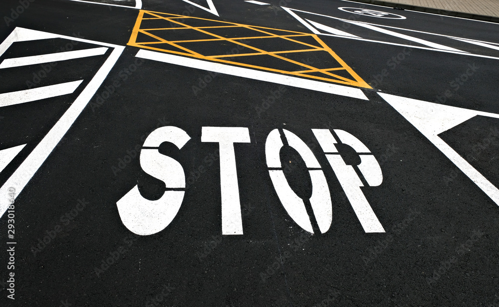 Road signage symbols and bold white word STOP painted on black pavement ...