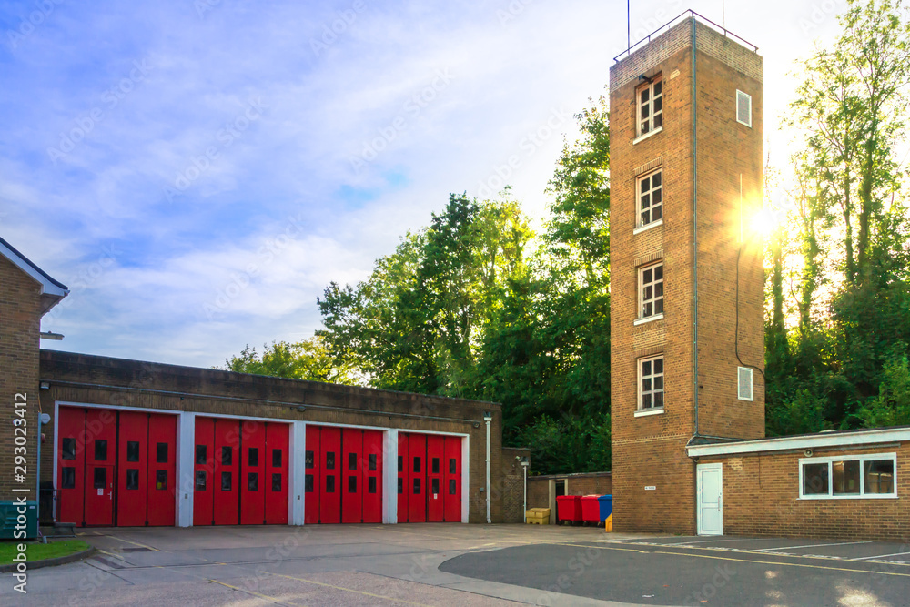 Facade of old fire station with red gates and tower close up against ...