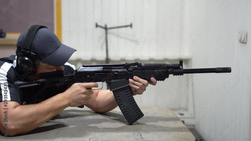 Stylish man shoots from a machine gun in the shooting gallery. Slow ...