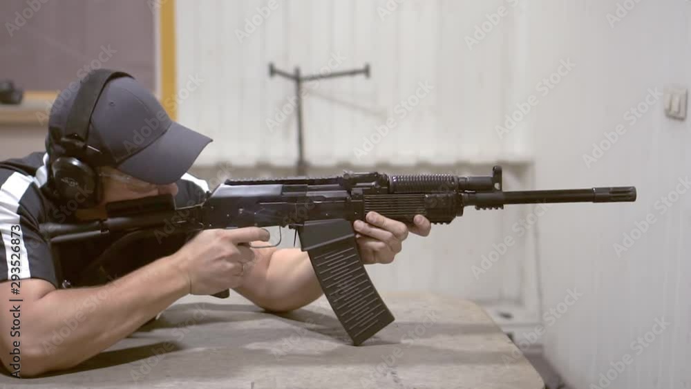 Stylish man shoots from a machine gun in the shooting gallery. Slow ...