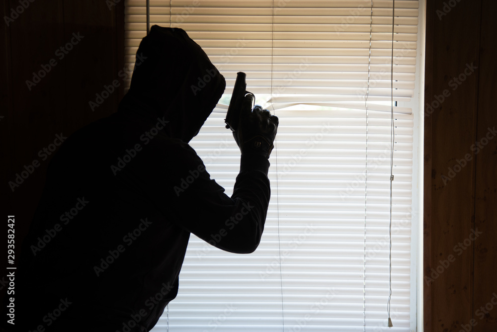 Criminal with gun is spying through the window. Robber breaking into ...